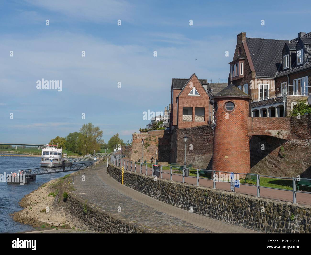 Historic brick buildings along a riverside footpath in sunny weather ...