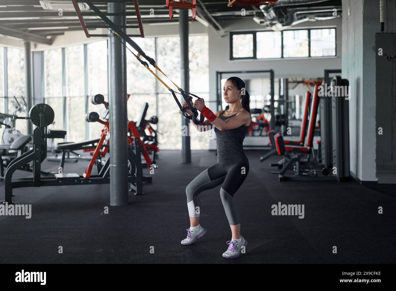 Full body of athlete woman training indoors with suspension system ...