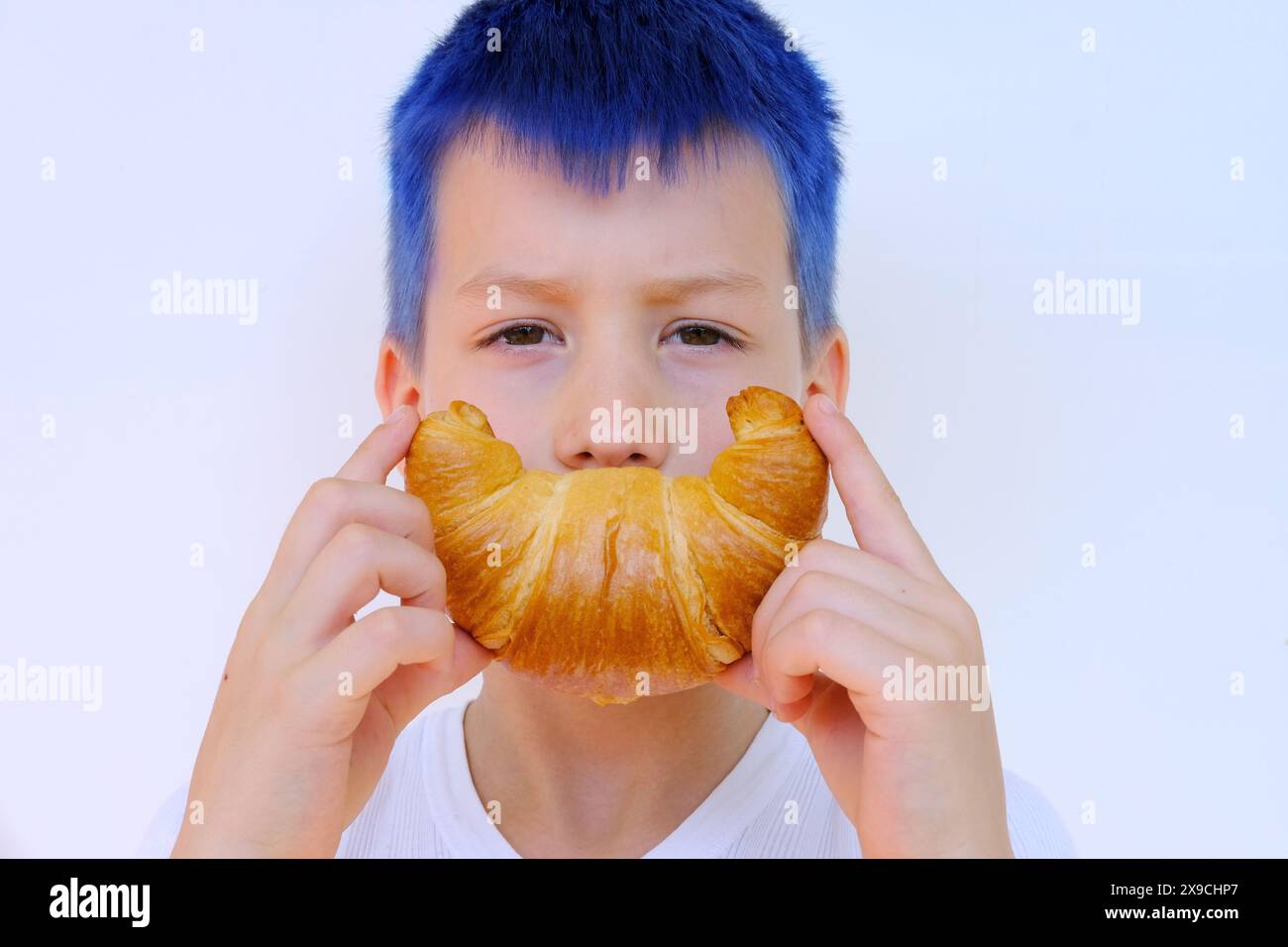 close-up of child's face, boy of 8 years old holds rosy baked croissant ...