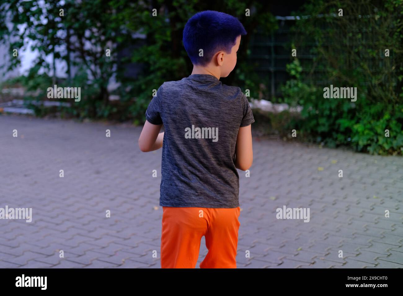 child, boy 8-9 years with blue hair stands with his back in the yard on natural green background ...