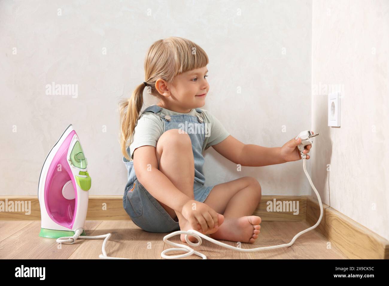 Little child playing with electrical socket and iron plug at home ...