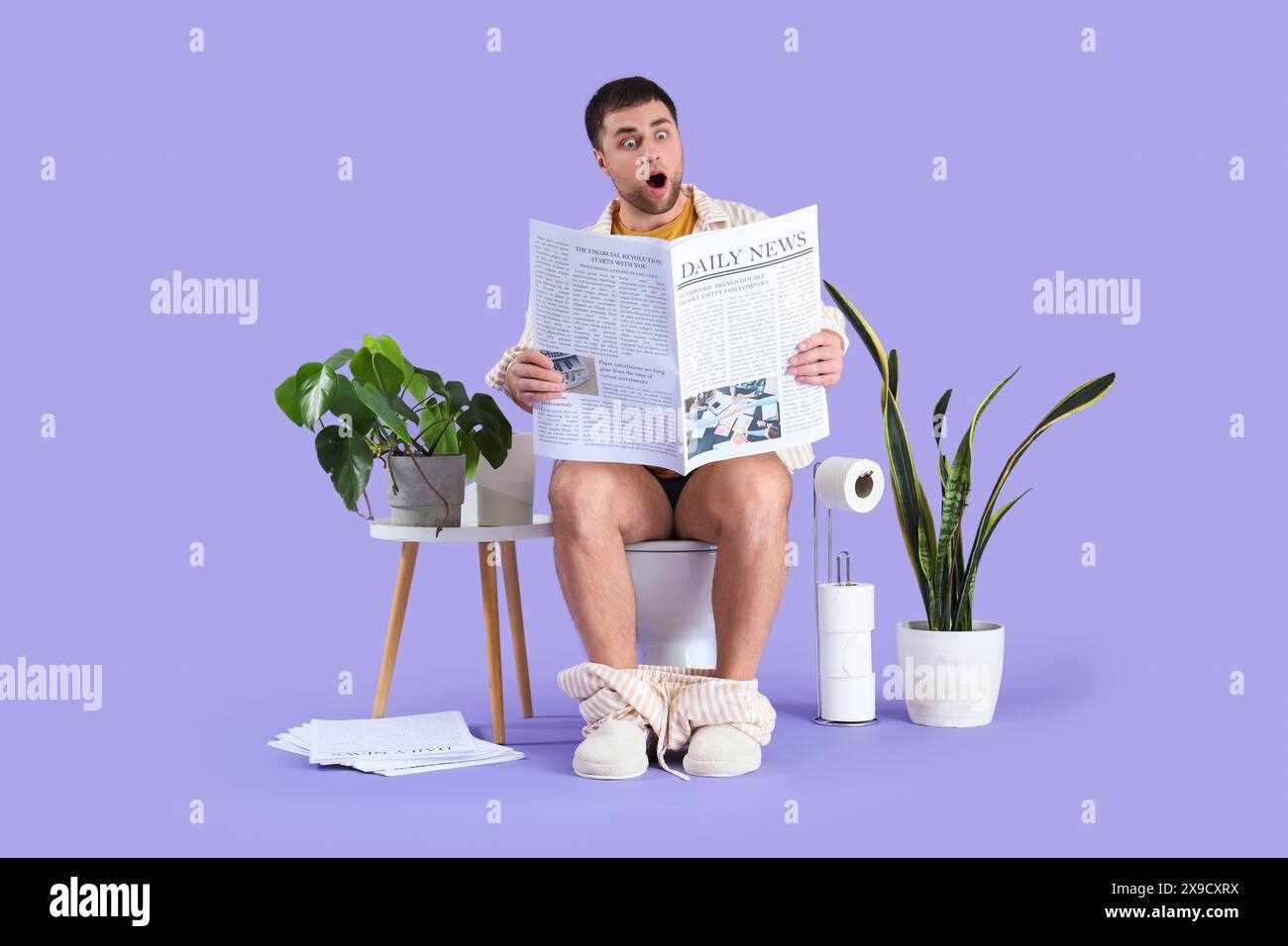 Shocked young man reading newspaper on toilet bowl against lilac ...