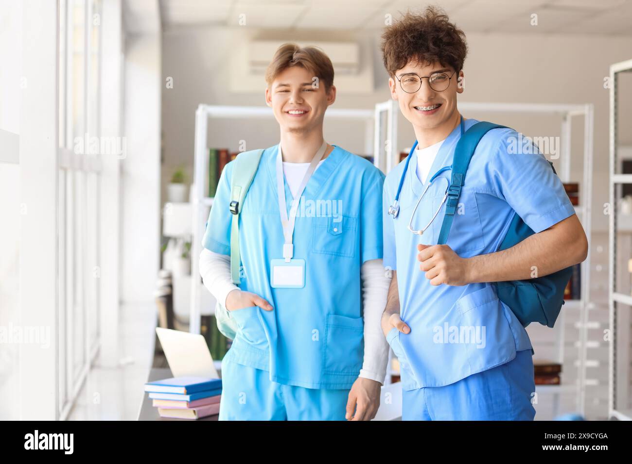 Male medical interns with backpacks near window in library Stock Photo ...
