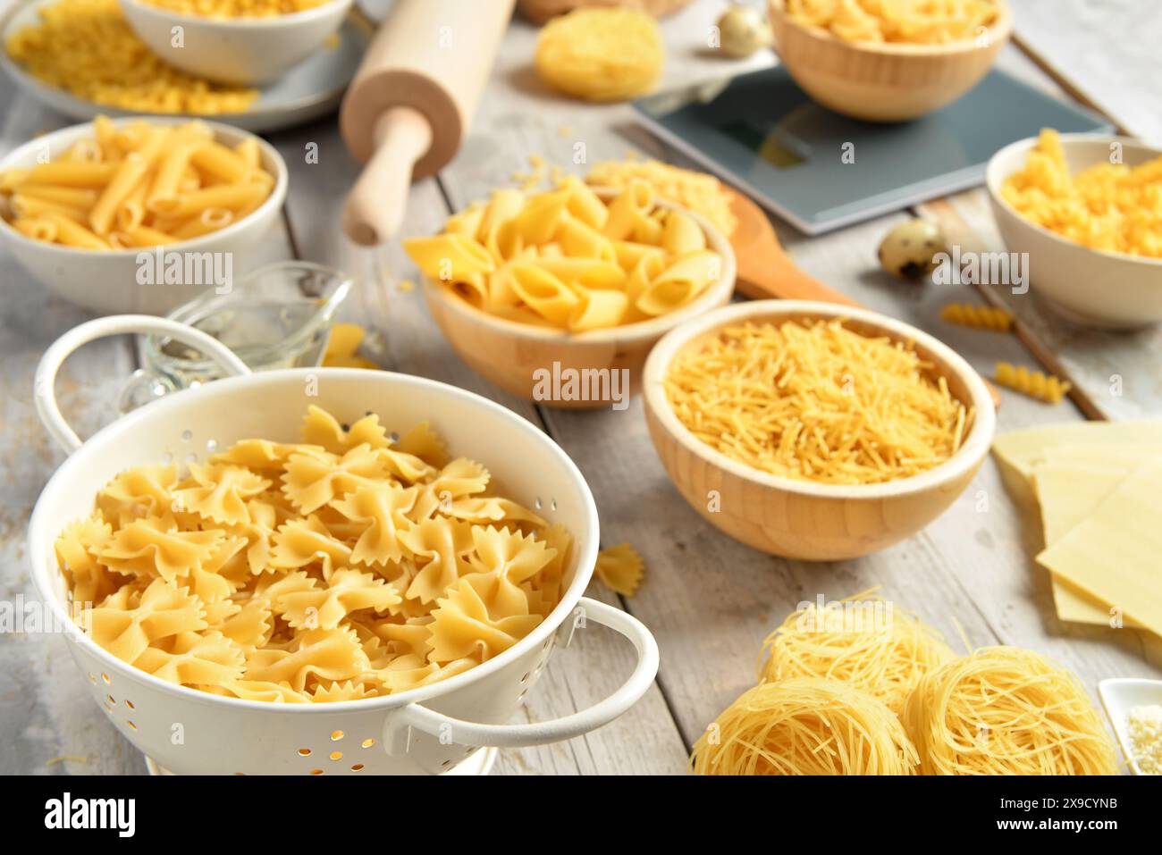Different types of raw pasta and kitchen utensils on light wooden ...