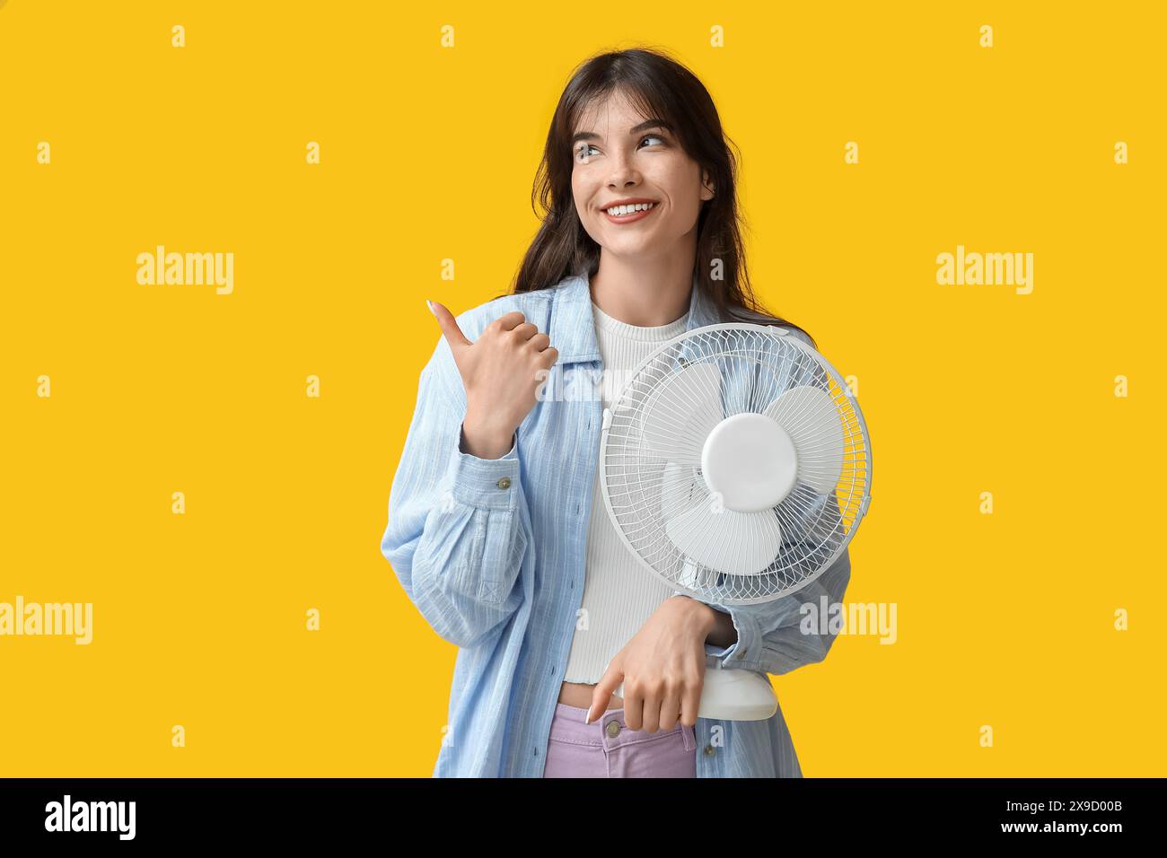 Young woman with electric fan pointing at something on yellow ...