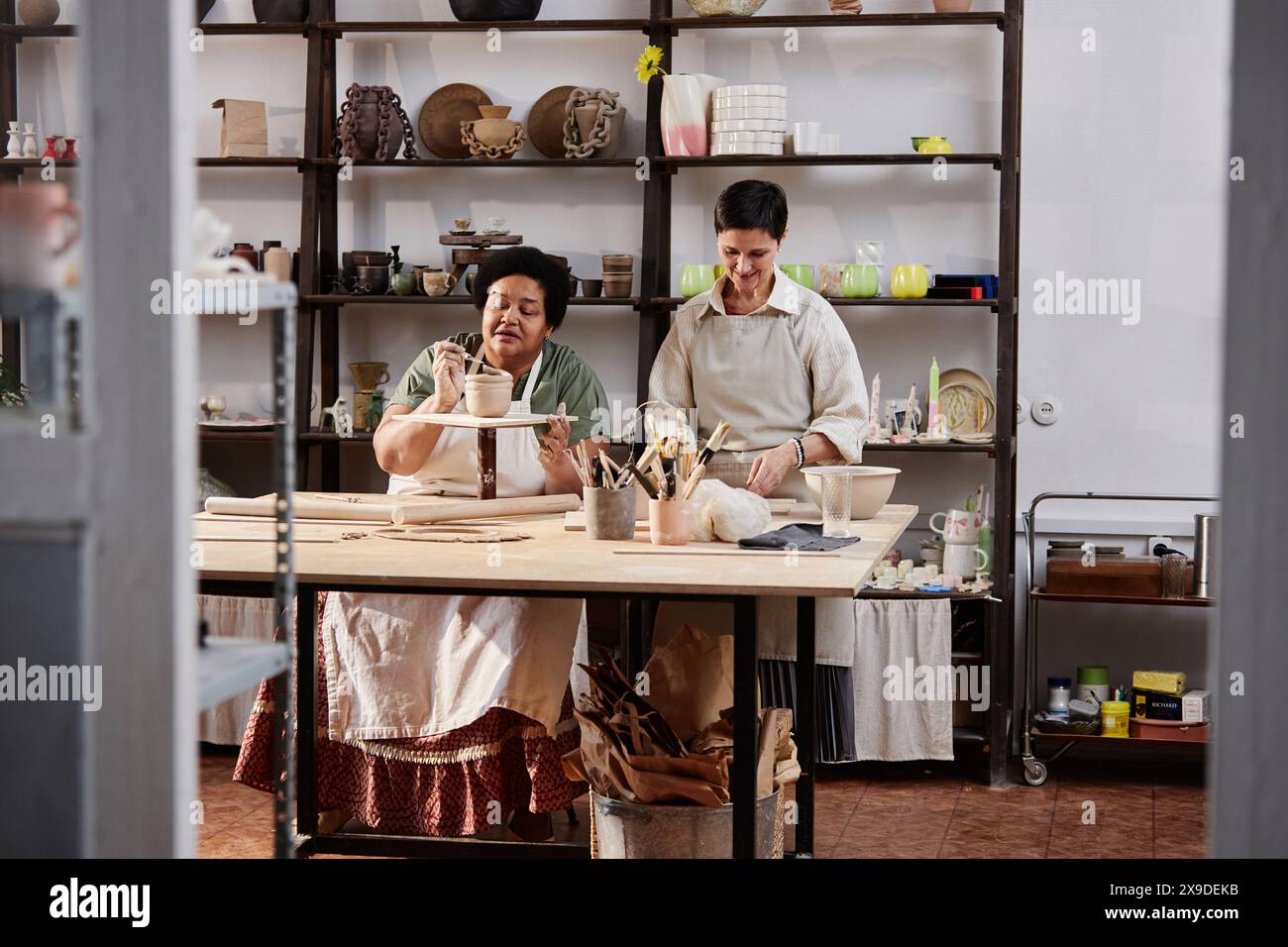 Wide angle view at two mature women enjoying pottery class and making ...