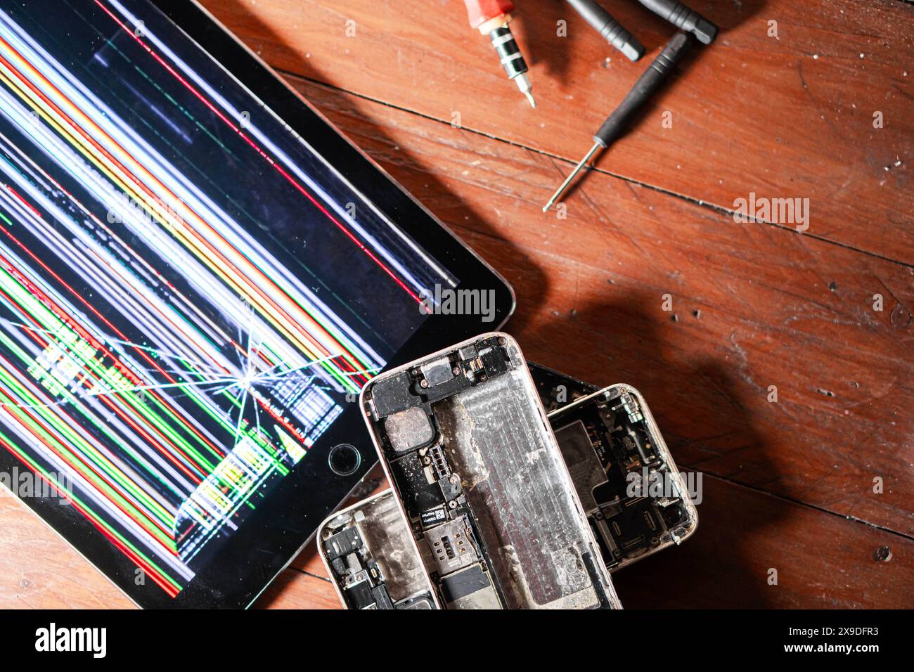 A broken tablet with a colorful, distorted screen and two disassembled ...