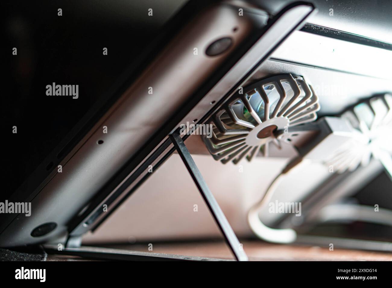 Close-up of a laptop on a stand with an external cooling fan attached ...