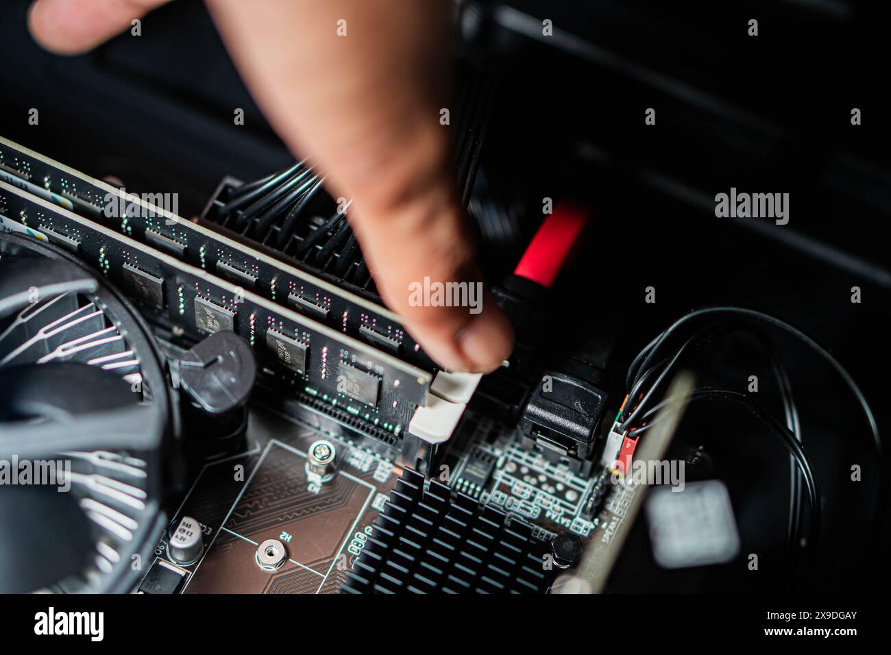 A close-up of a person's hand installing or adjusting a RAM module on a computer motherboard ...
