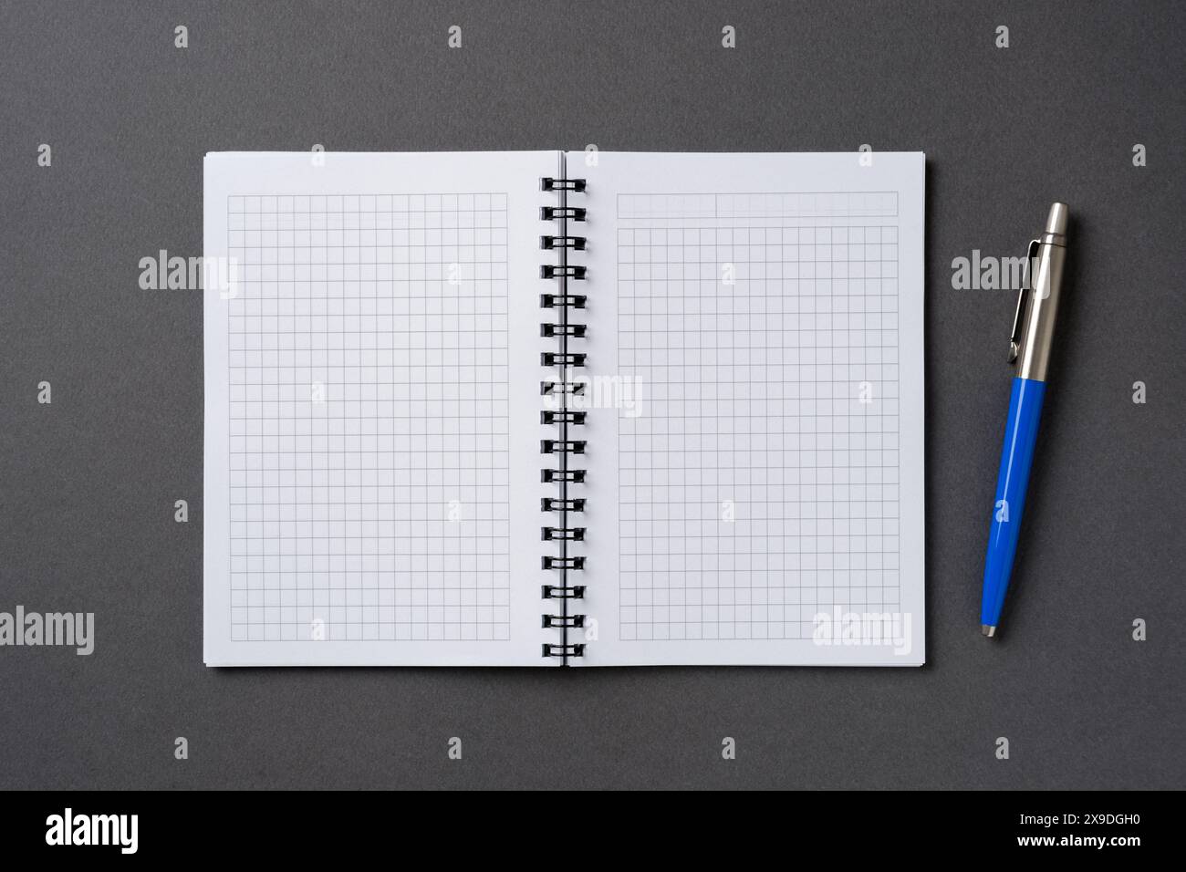 Checkered and spiral notebook on a dark gray table with a ballpoint pen ...
