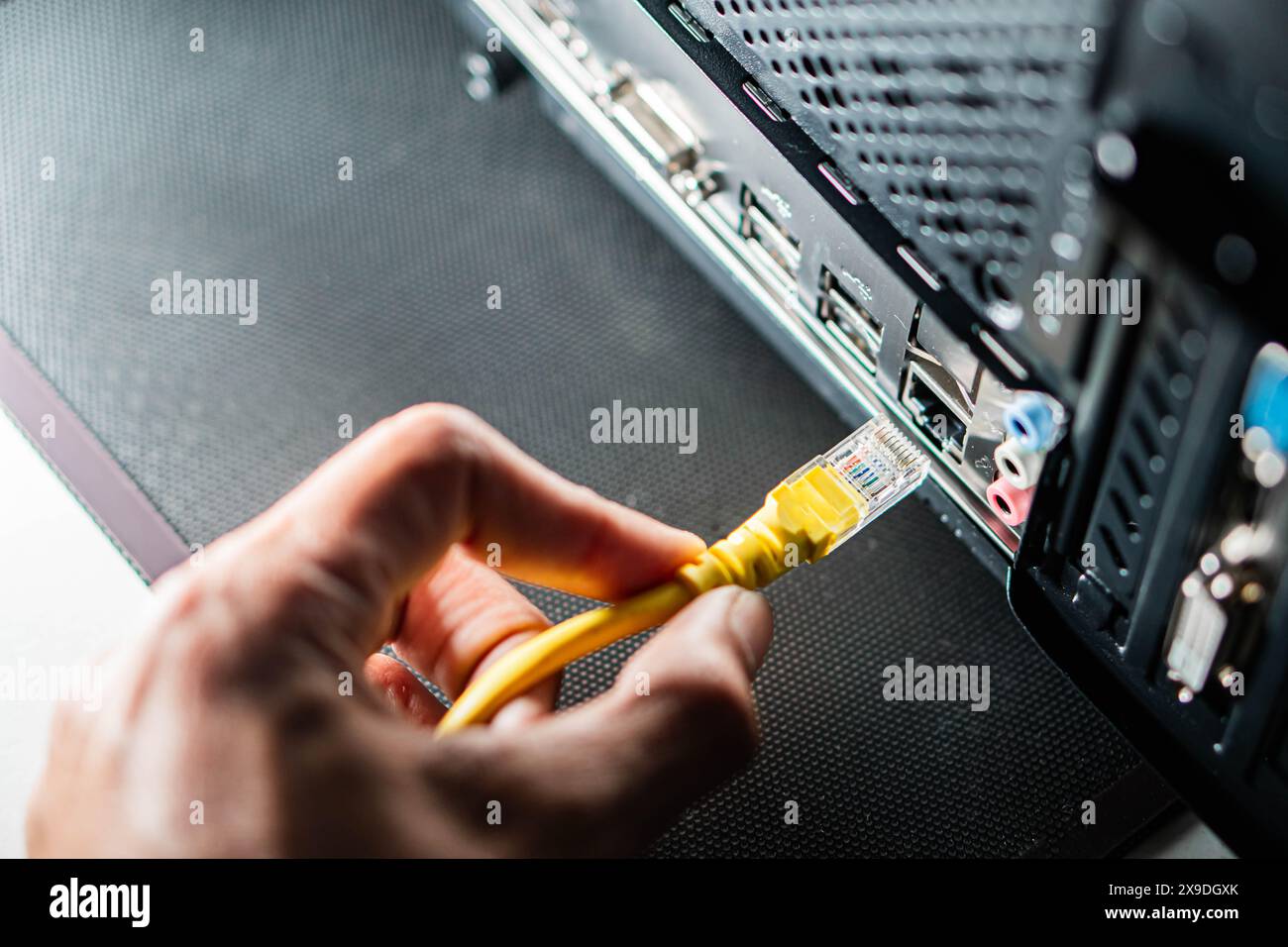 A person plugging a yellow Ethernet cable into the back of a computer ...