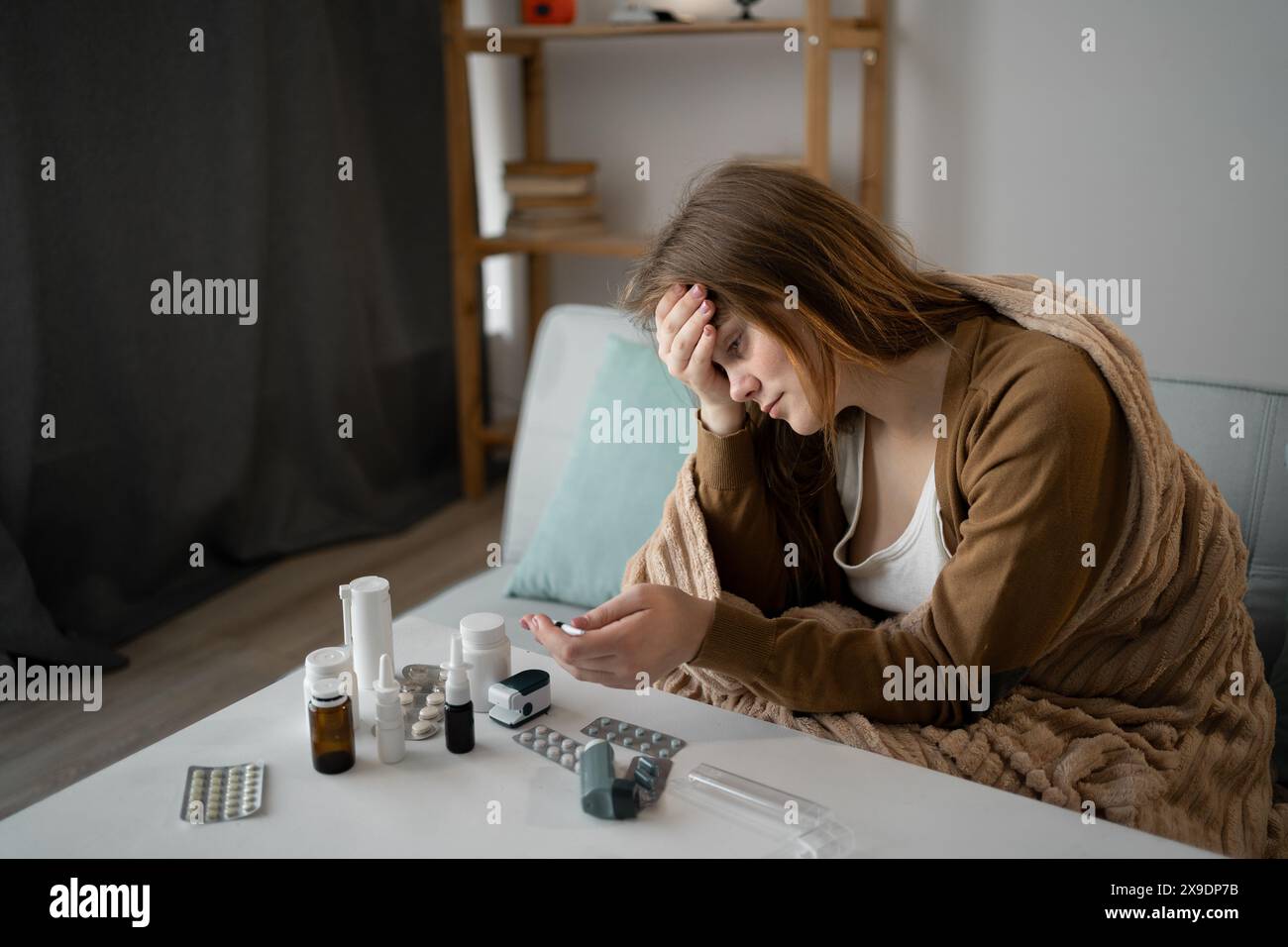 A sick woman is wrapped in blanket on the sofa. Suffering from flu-like ...