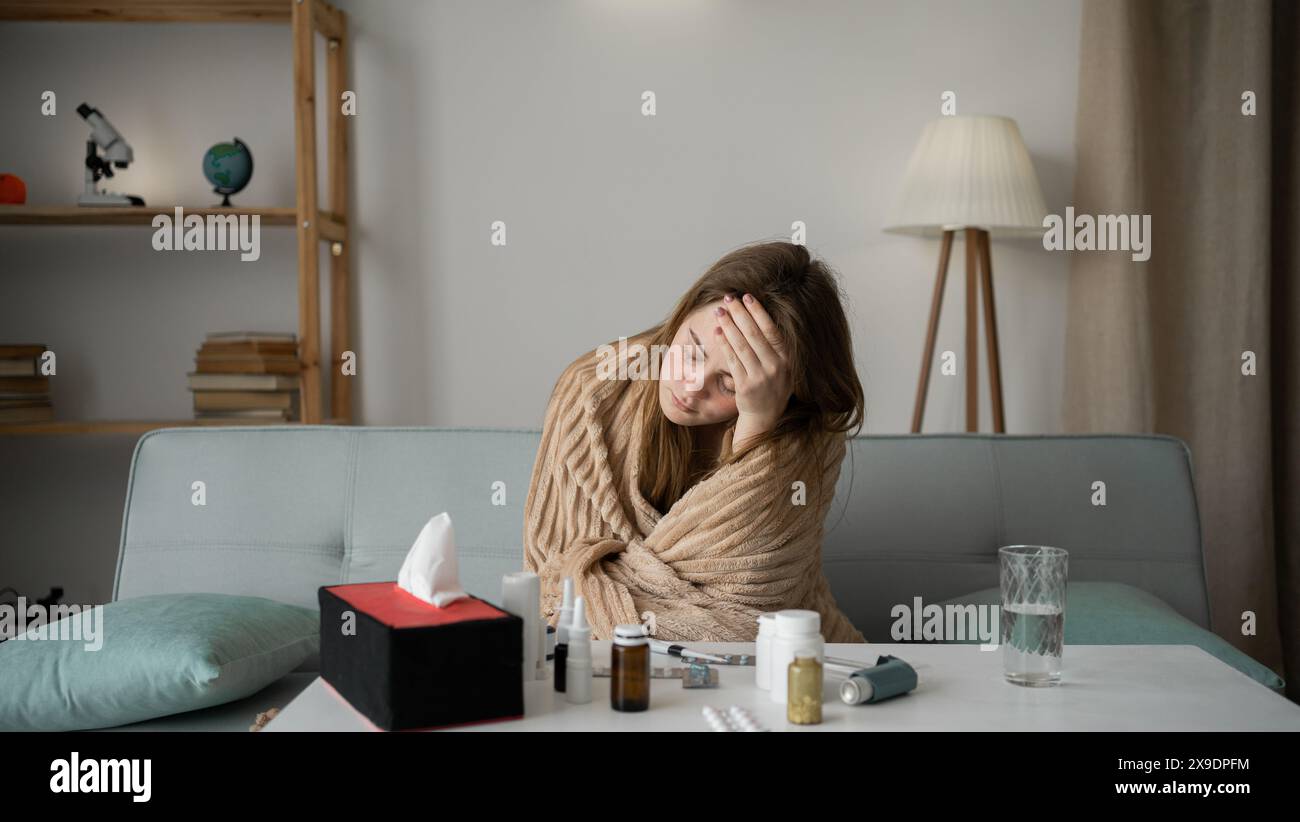 young sick woman sits on the sofa at home, bends over a table with ...