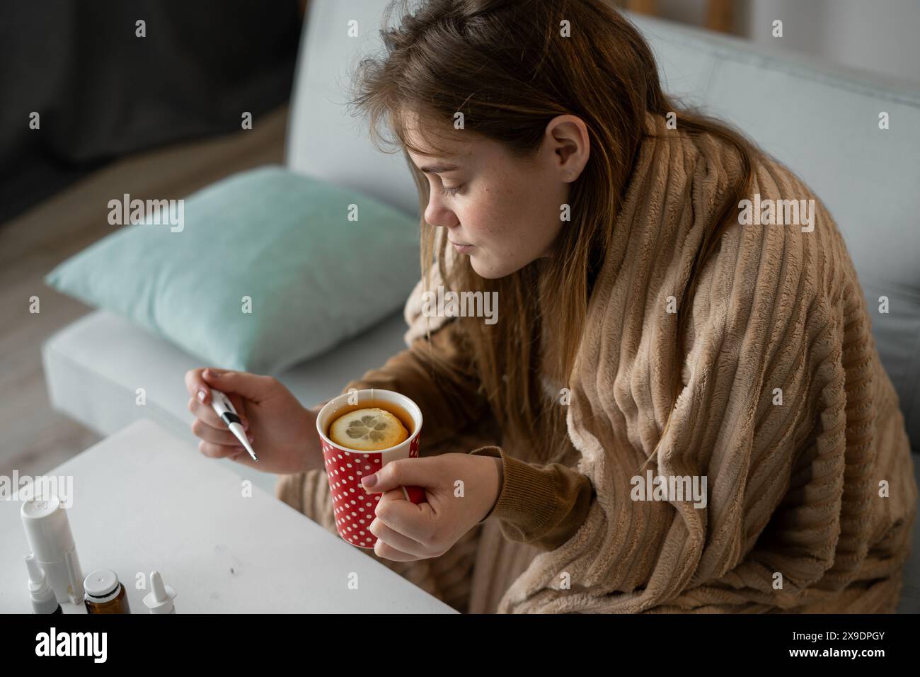 sick woman takes her temperature and drinks tea with lemon for cold ...