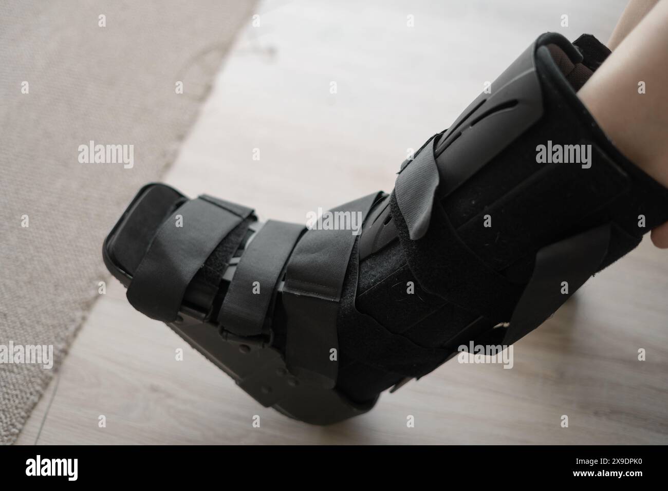 Close-up of female leg with black splint, walker boot, orthosis, sprained ankle at home. Ankle ...