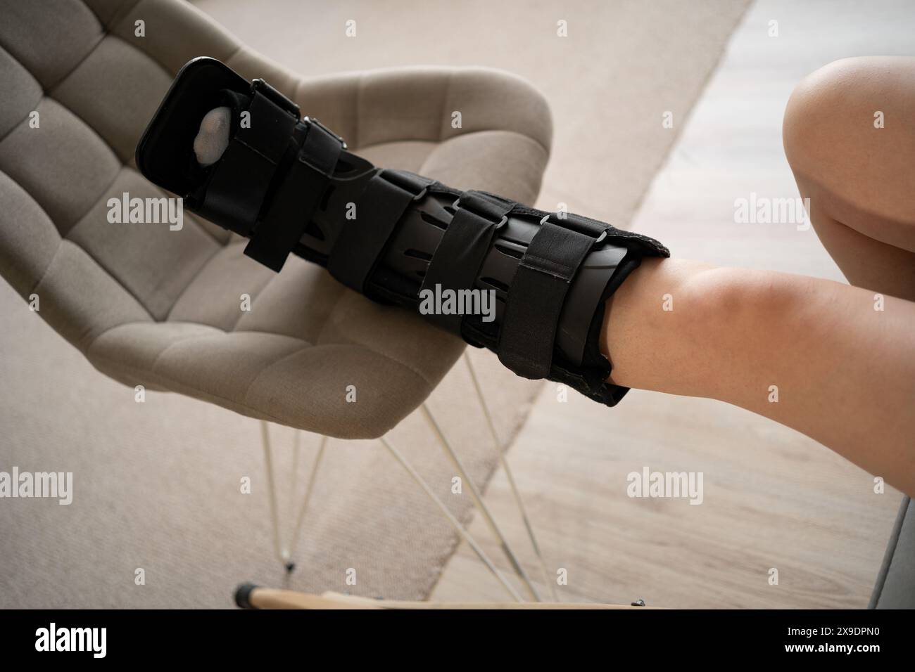 injured woman with black splint on her leg leans on chair home. Ankle ...