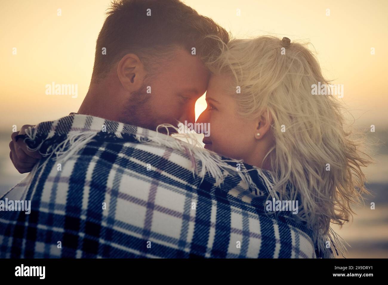 Couple, hug and blanket at beach, sunset and eye contact for connection ...