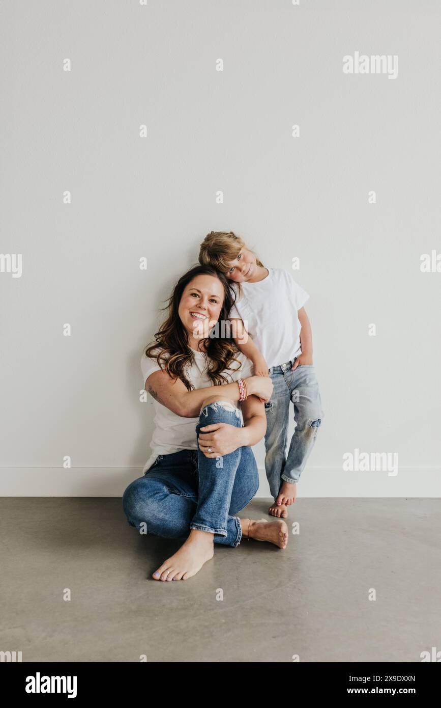 Mom sits on floor against wall while daughter stands and leans head ...
