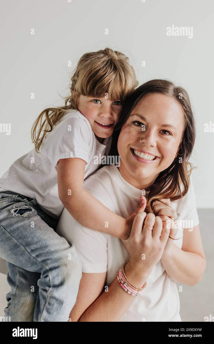 Young daughter hugs smiling mom from behind in studio Stock Photo - Alamy
