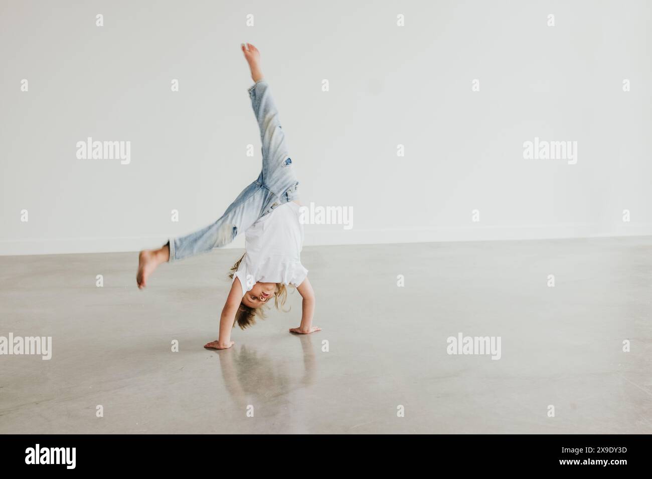 Young girl in blue jeans and t shirt does cartwheel in empty room Stock ...