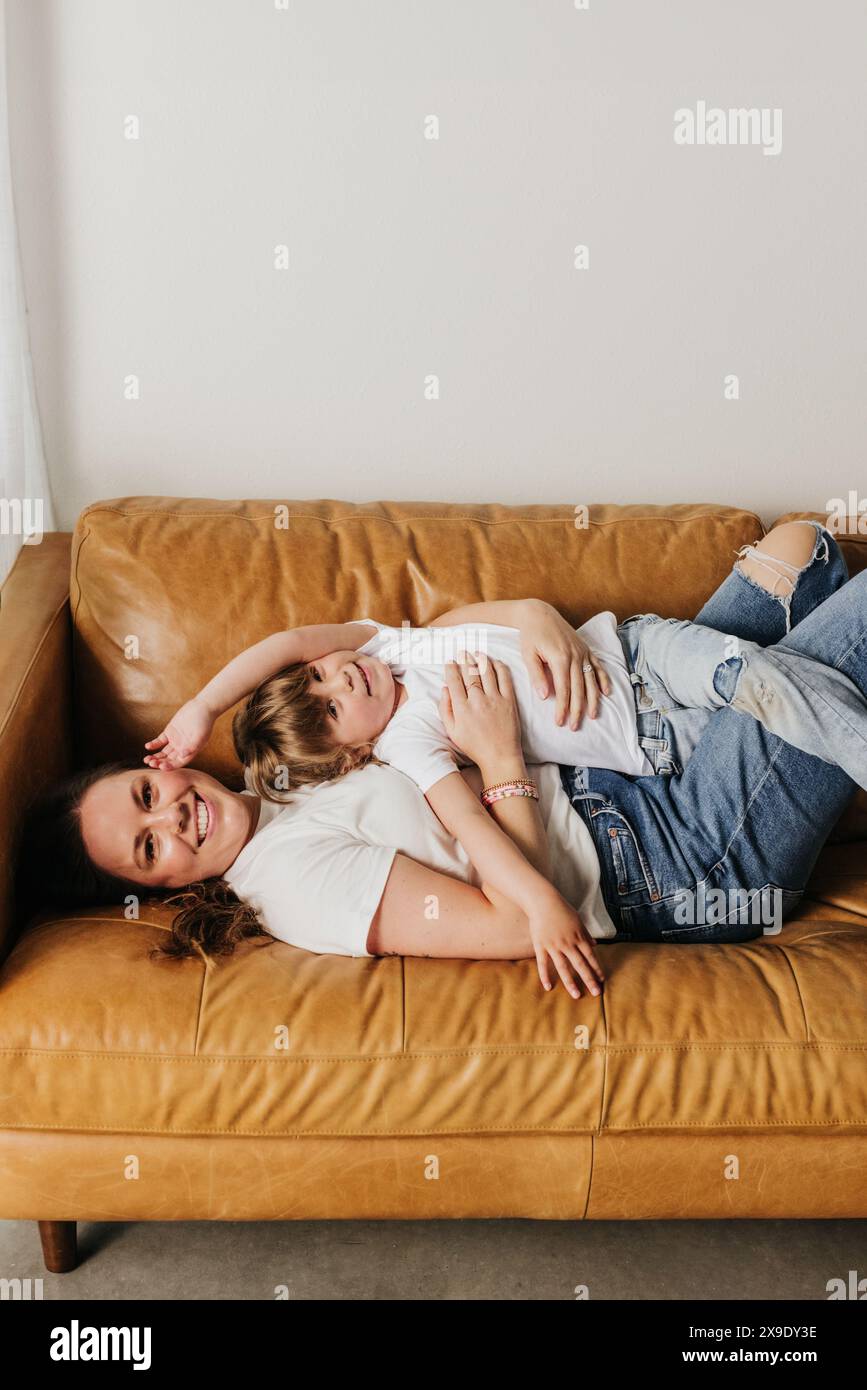 Mother and daughter snuggle on leather couch while smiling Stock Photo ...
