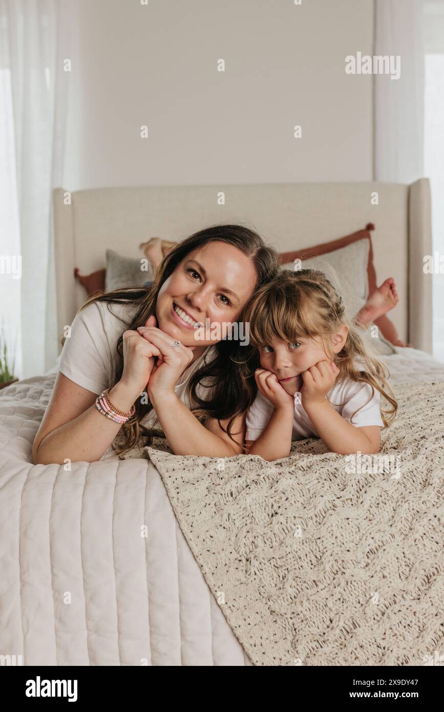 Mom and daughter lay on bed together while resting heads on hands Stock ...
