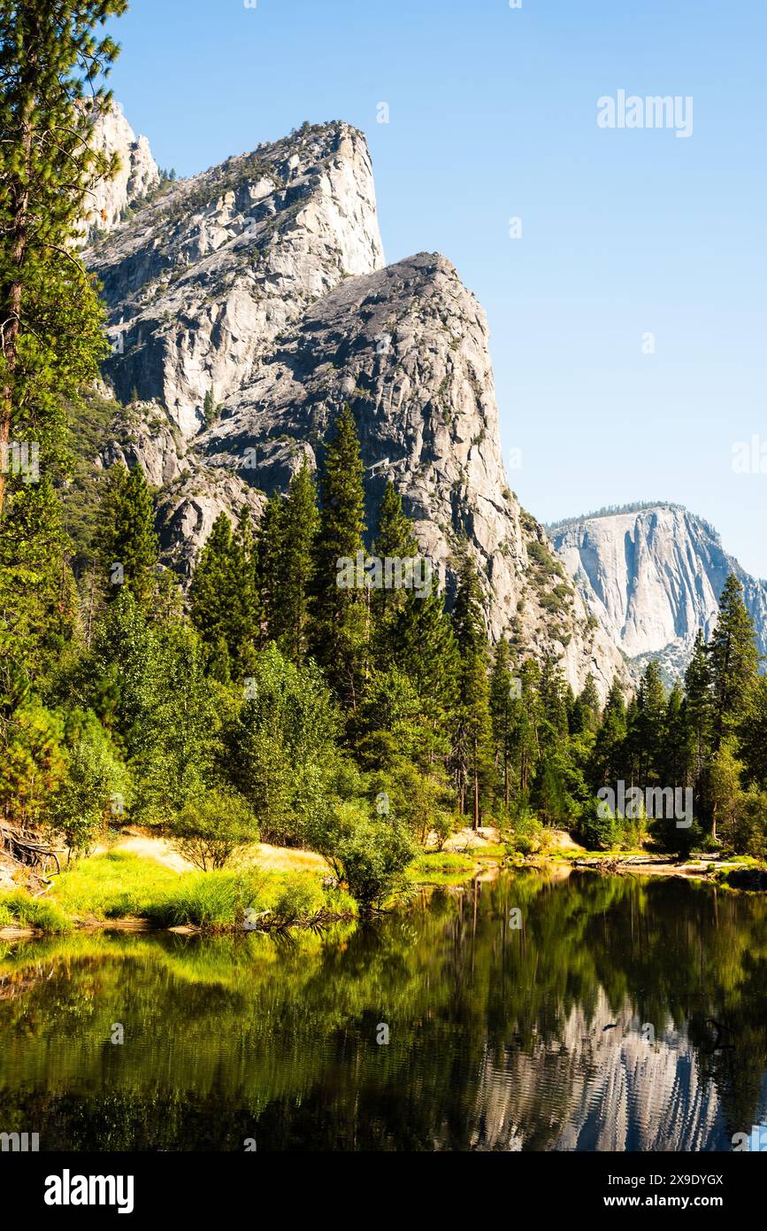 Yosemite granite cliffs reflecting in a calm river surrounded by pines ...