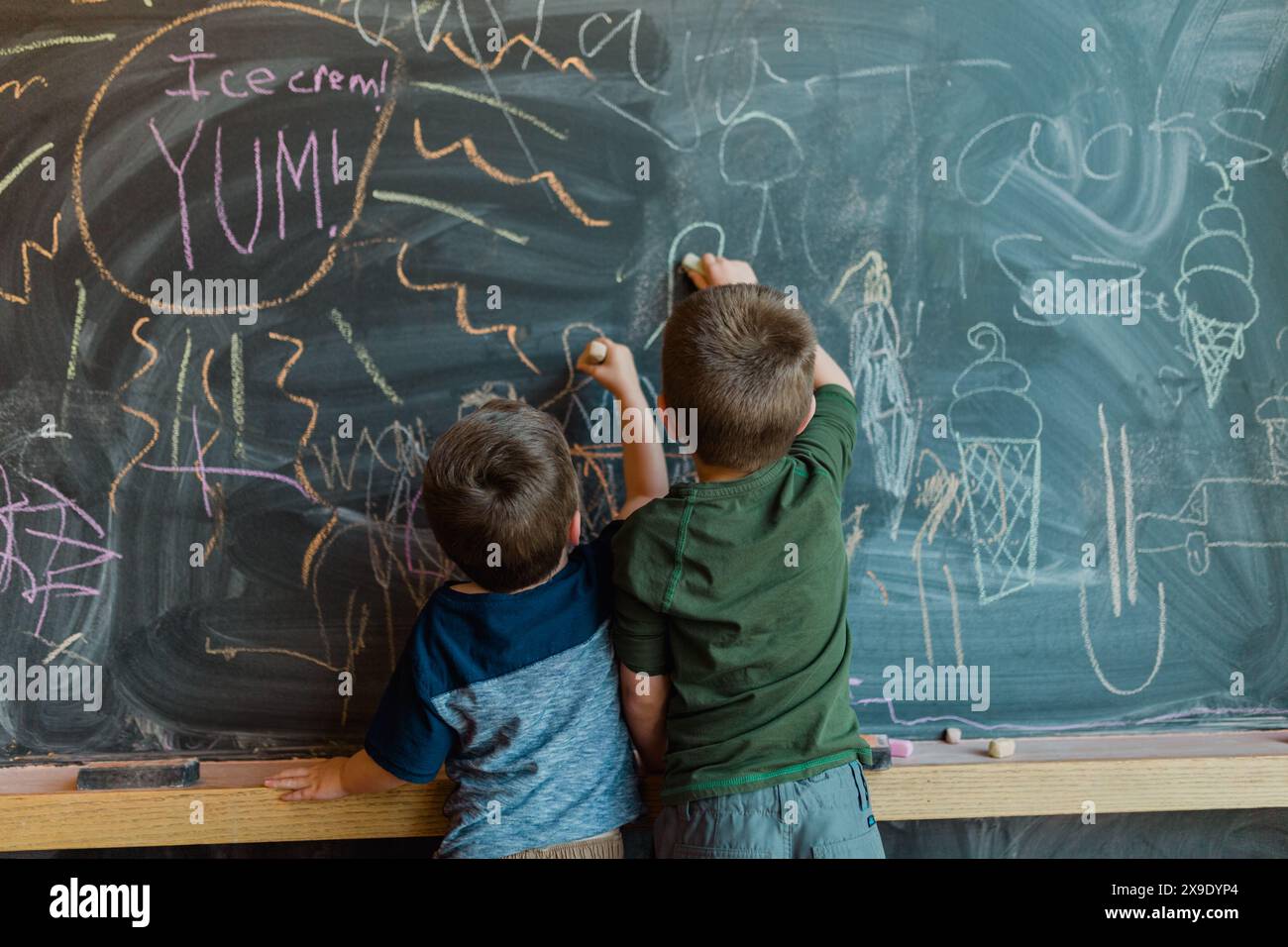 Two young brothers drawing colorful pictures on a large chalkboard ...