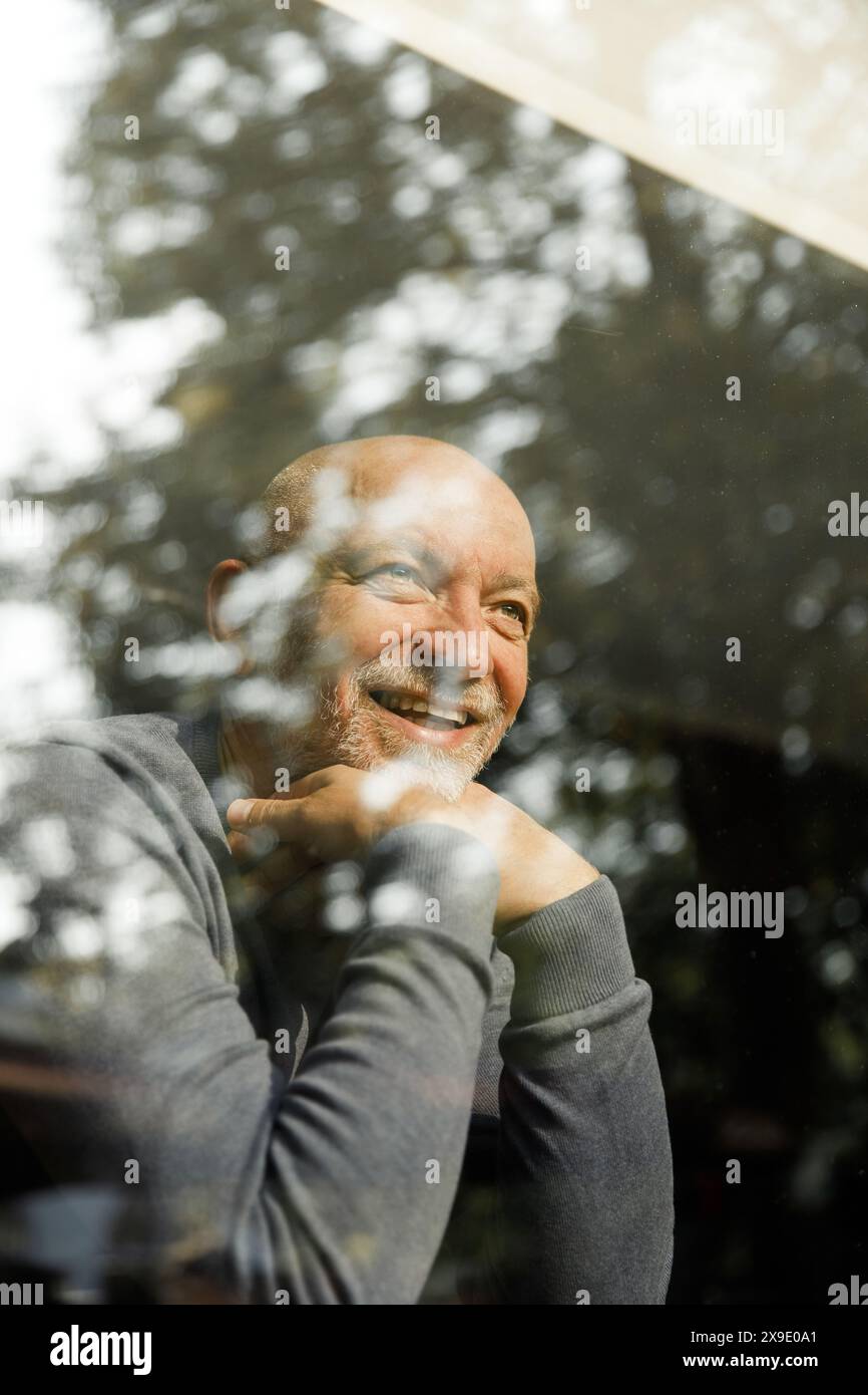 Elderly man smiling with hands on chin behind a reflective window Stock ...