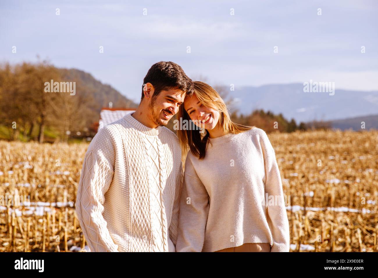 Young couple leaning heads together, standing in a harvested field ...
