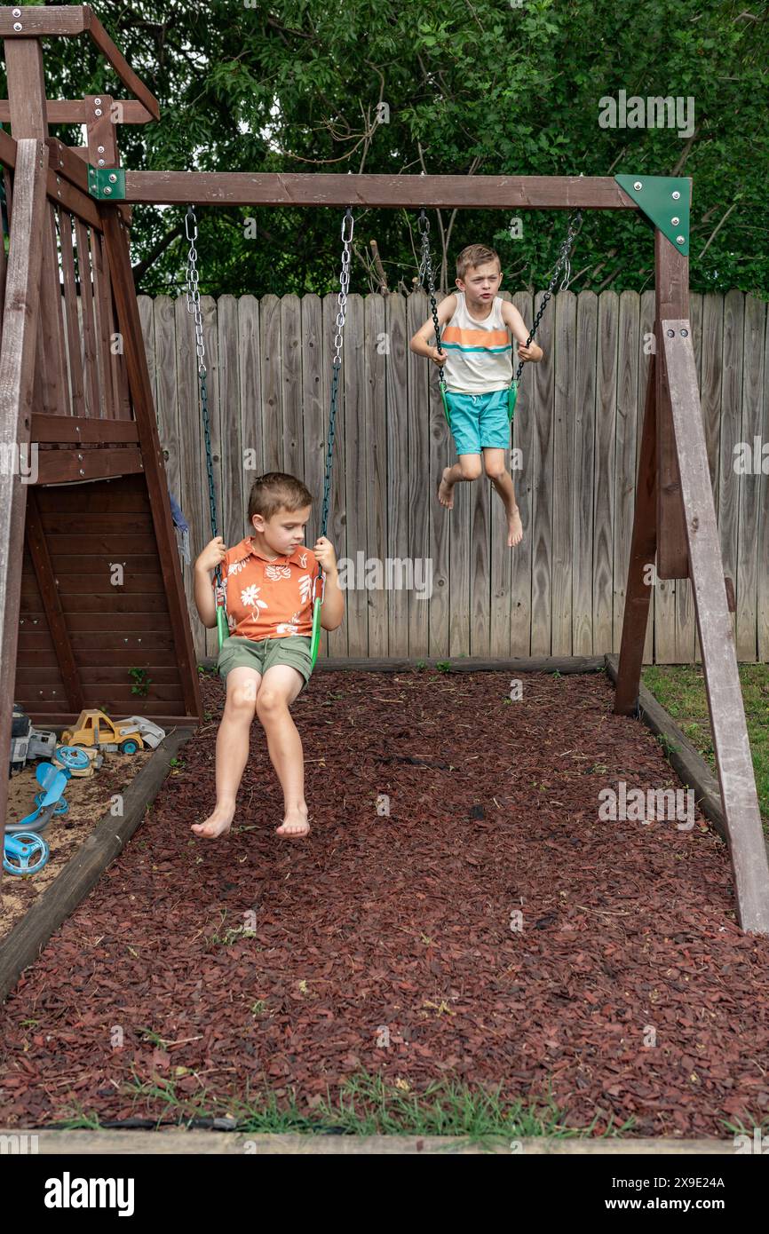 two brothers swinging on backyard play set in the summer Stock Photo ...