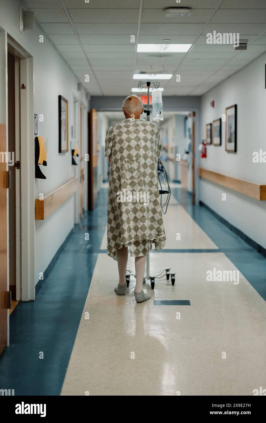elderly male cancer patient wearing gown walks down hall in hospital ...