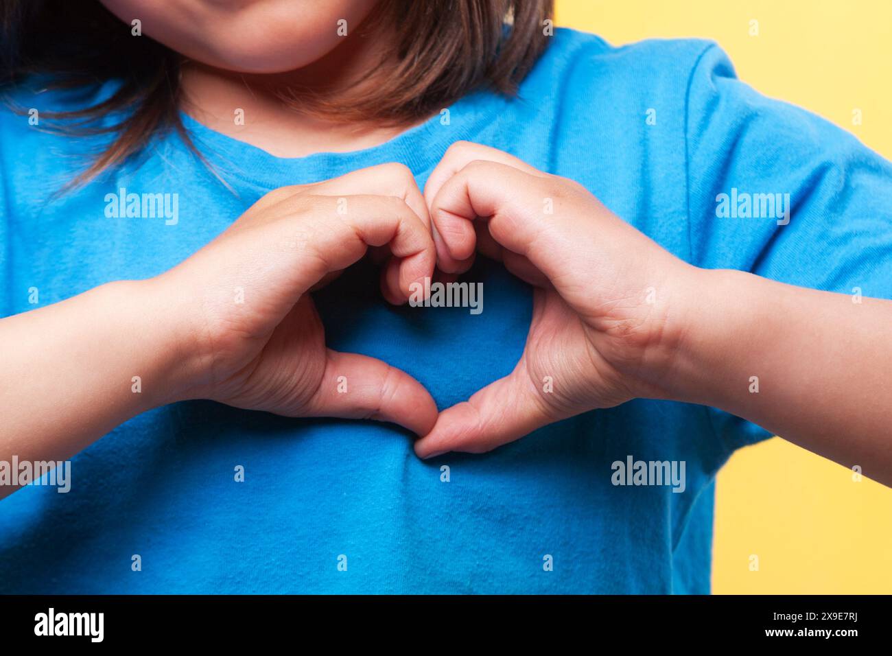Close-up child hands on the chest in the shape of a heart. Blue T-shirt ...
