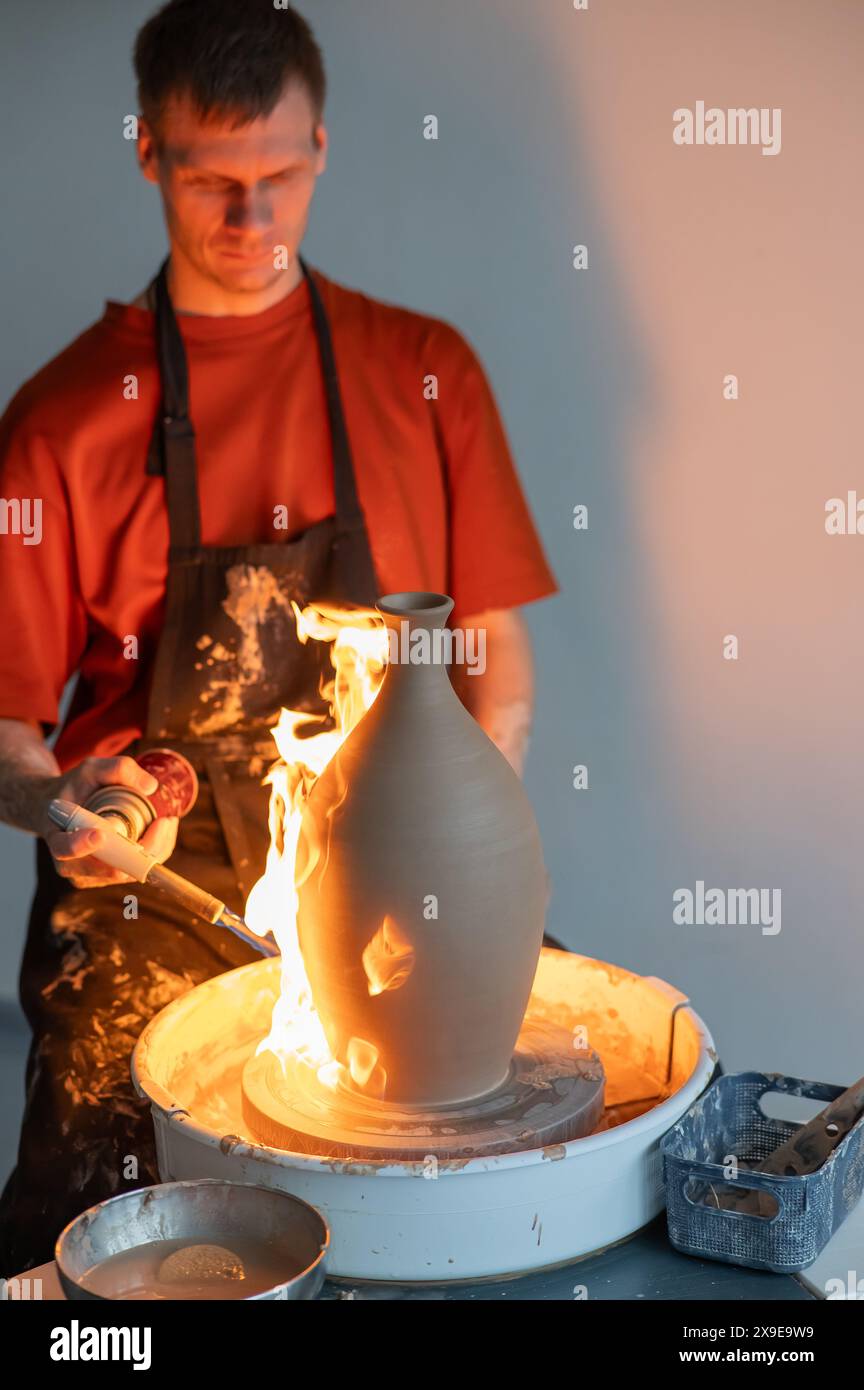A potter burns a jug with a gas burner on a potter's wheel. Vertical ...