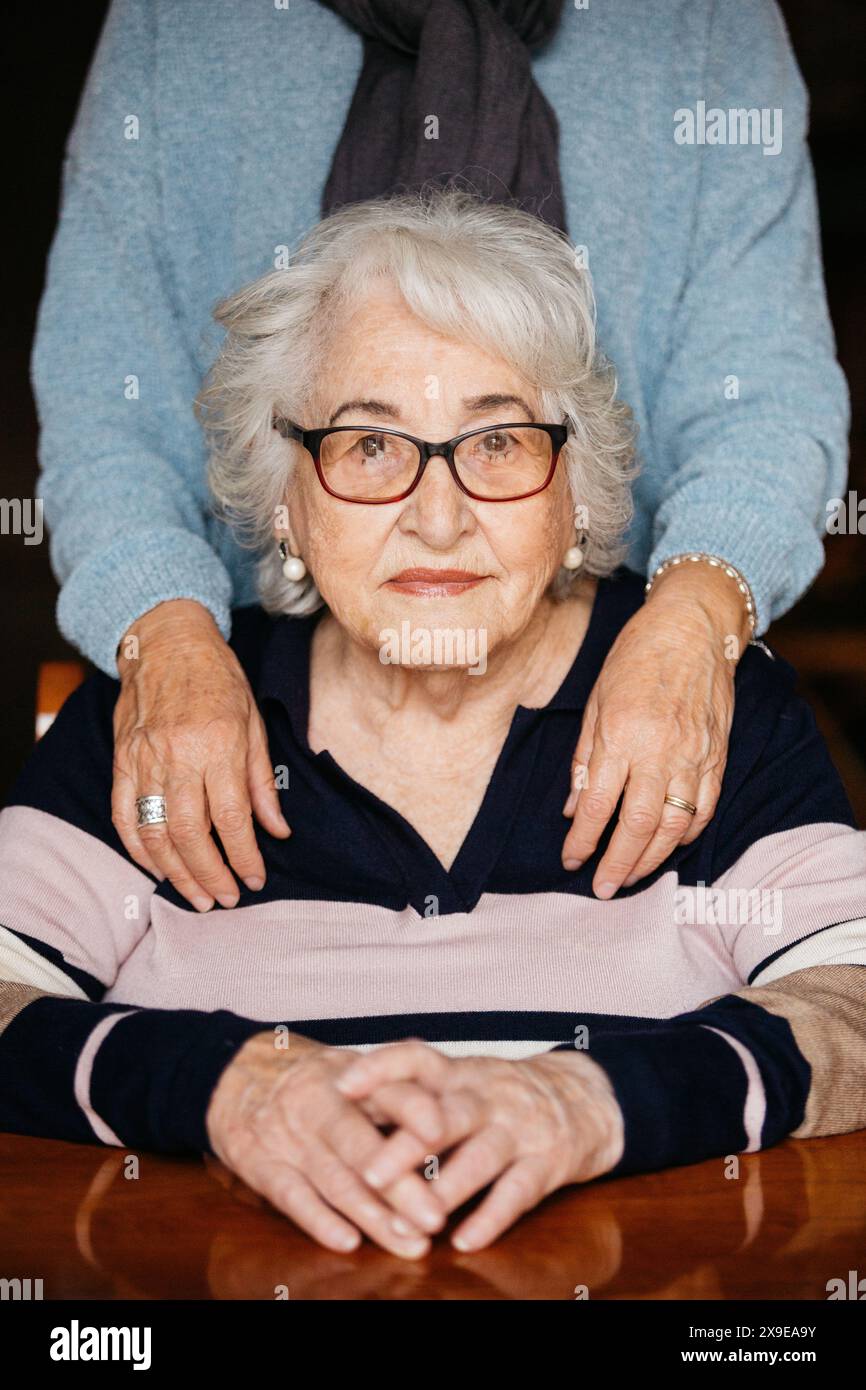 Portrait of an elderly woman sitting at a table with her hands folded ...