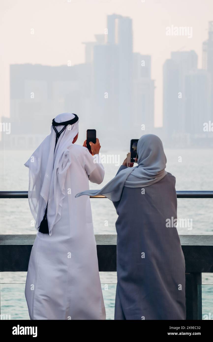 A couple wearing traditional Qatari clothes looks at the Doha skyline ...