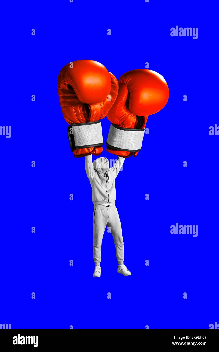 Young man in sportswear raising giant fists in boxing gloves on blue ...
