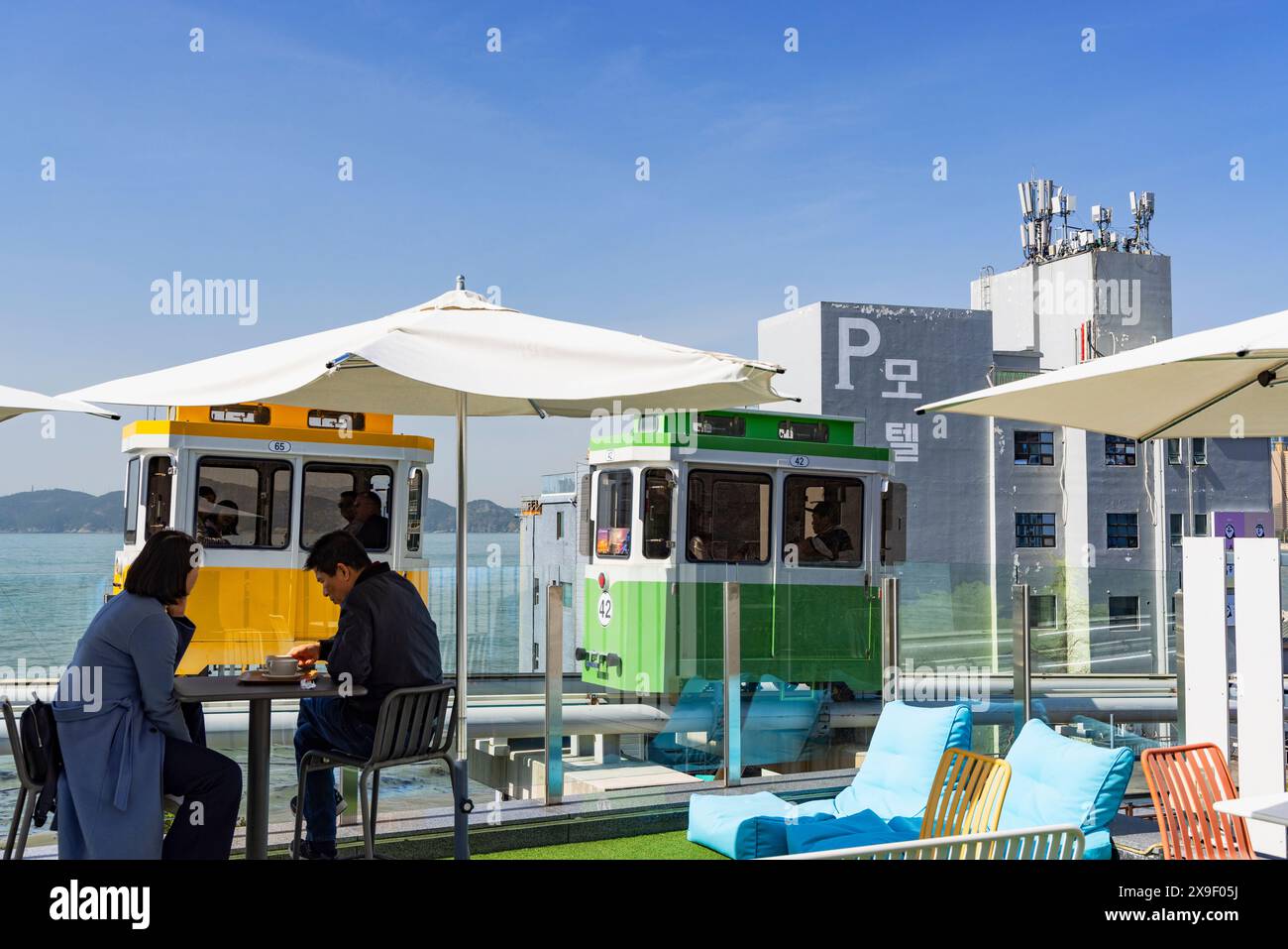 Cars of Haeundae Blueline Park passing outdoor cafe, Haeundae Beach ...