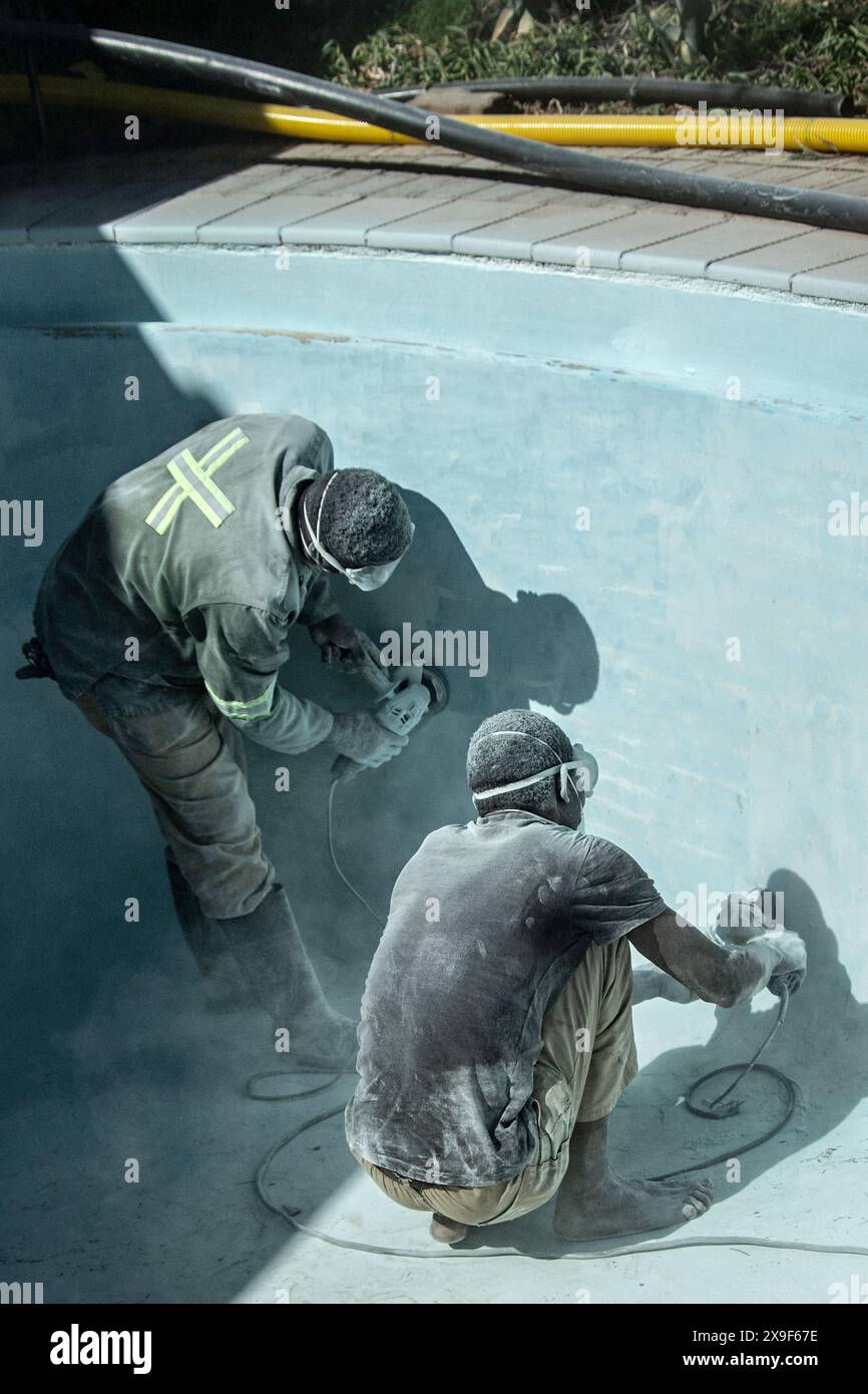Two workmen grinding out bubbles in old fibreglass.swimming pool Stock ...