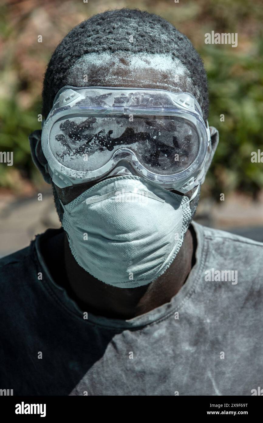 A construction worker covered in white dust from grinding with mask and ...