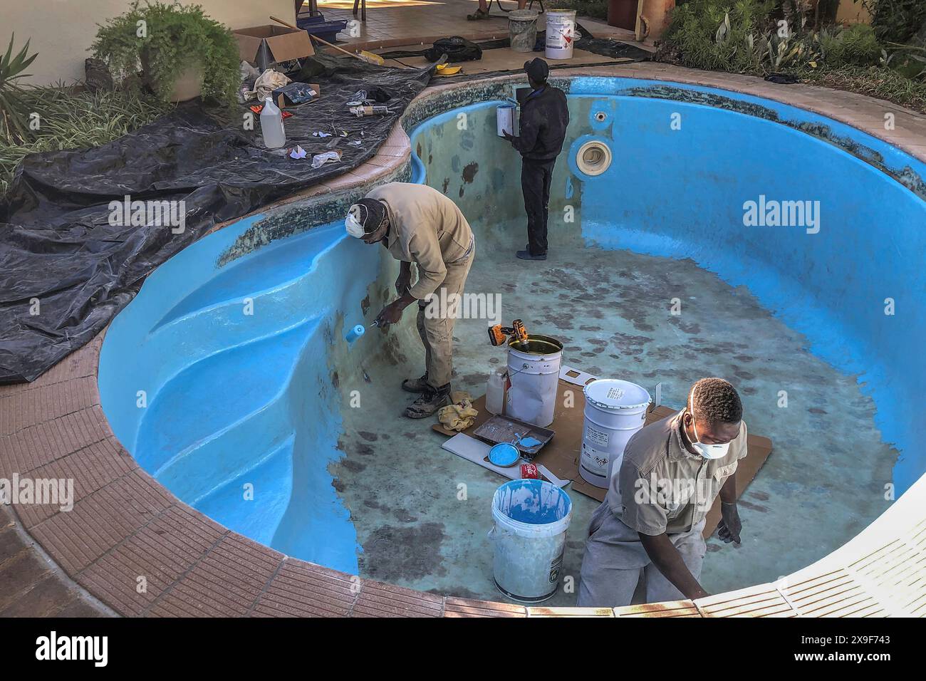 Workman using rollers and a paintbrush to apply fibreglass gel coat ...