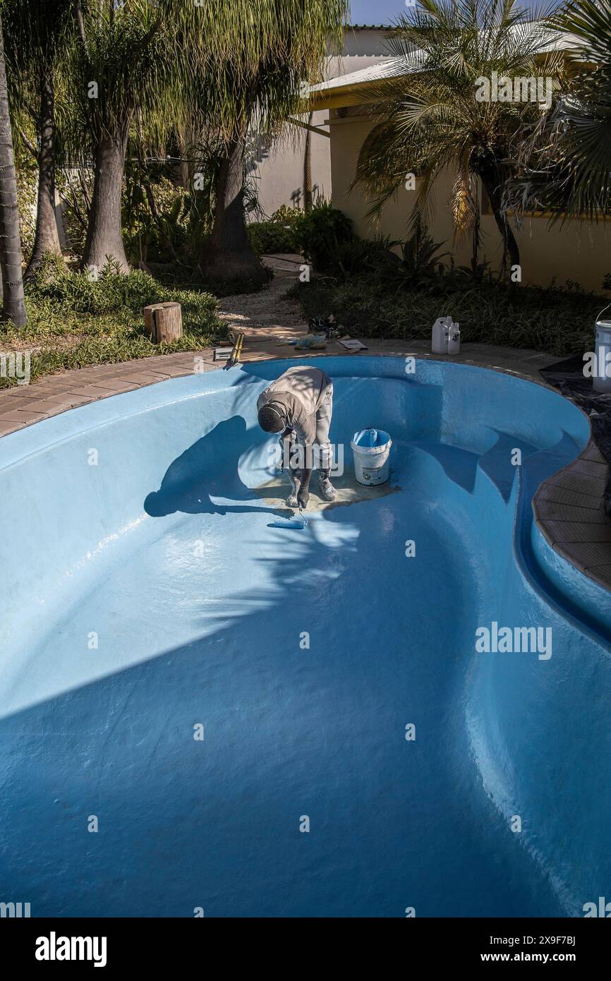 Workmen finishing off using roller to paint an old swimming pool with a ...
