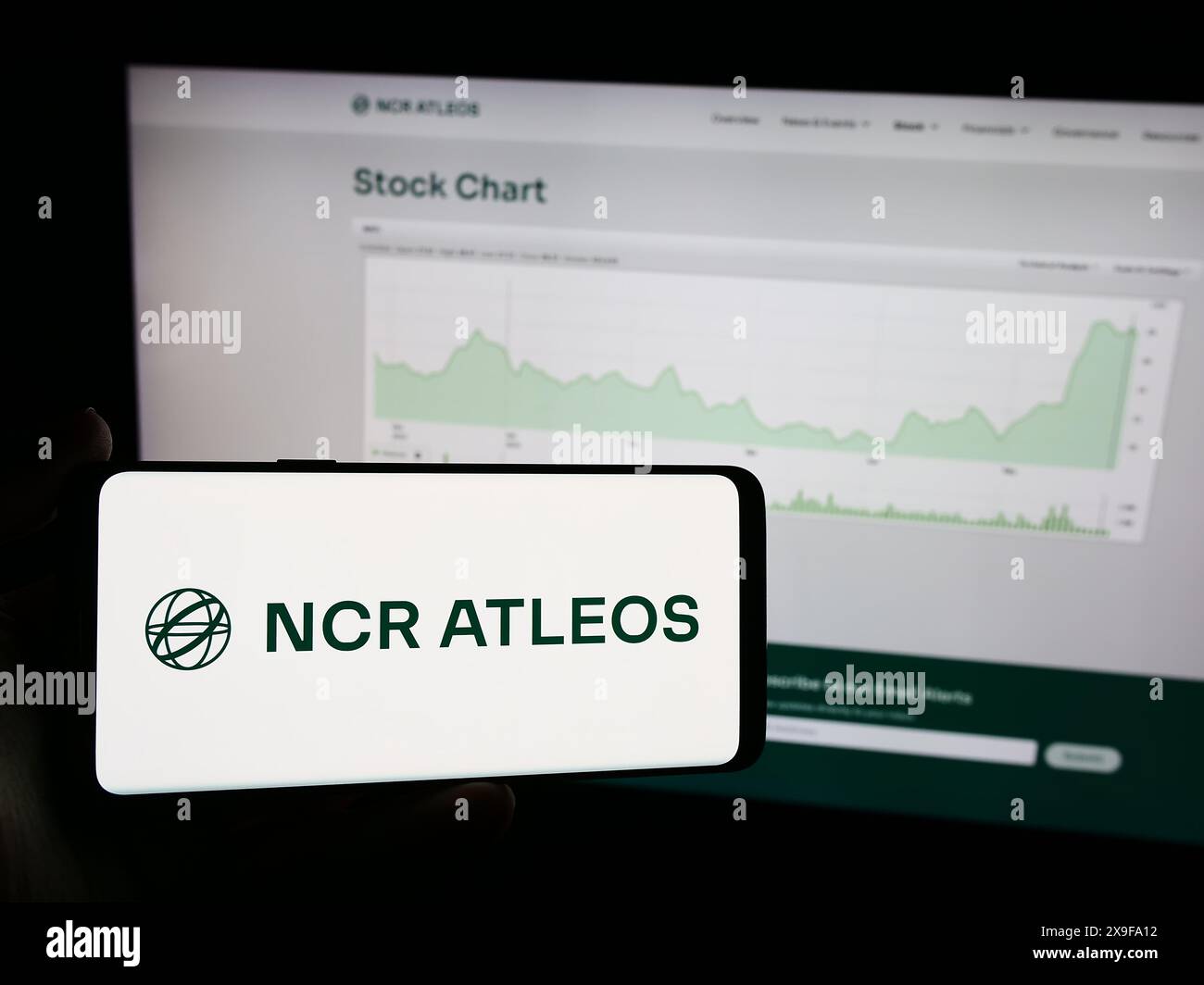 Person holding mobile phone with logo of US financial services company NCR Atleos Corporation in ...