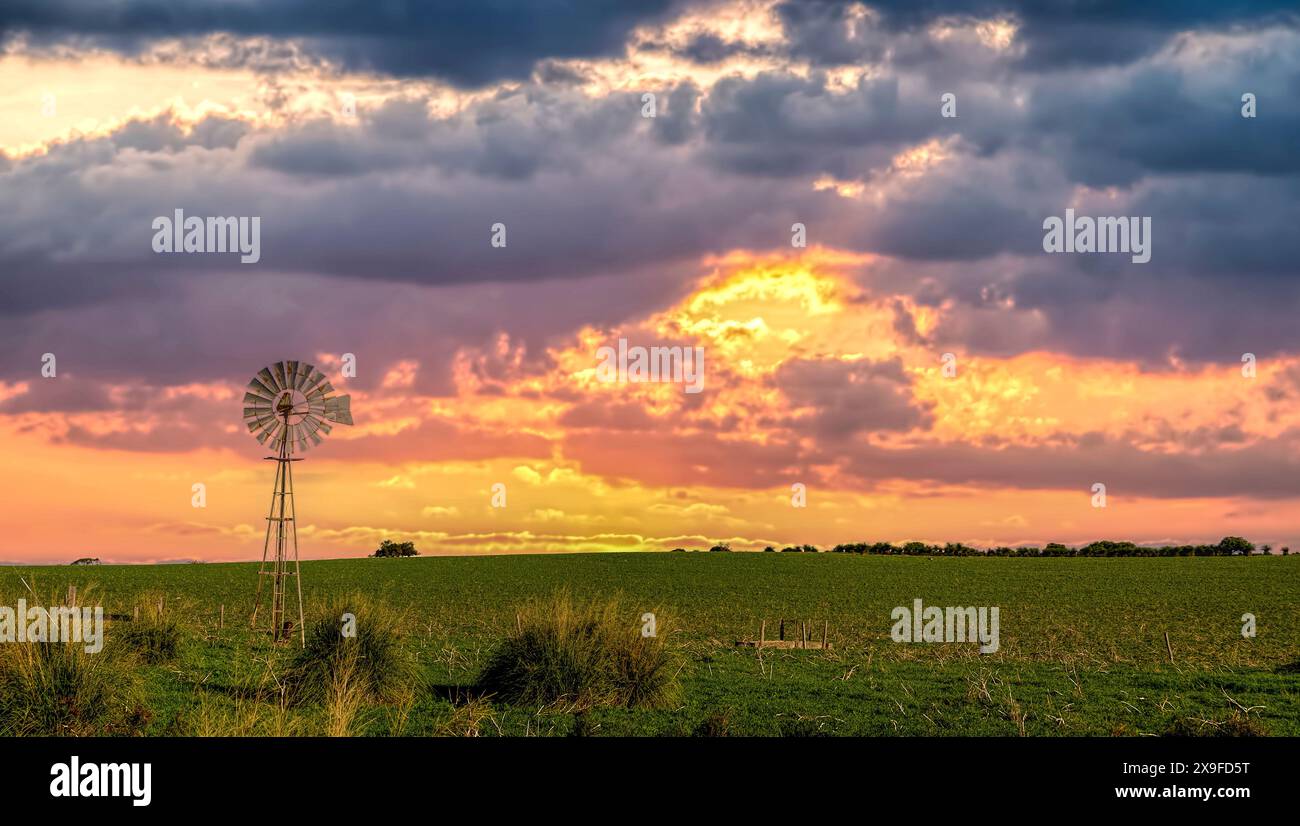 Sunset over a traditional metal windmill in rural outback landscape ...