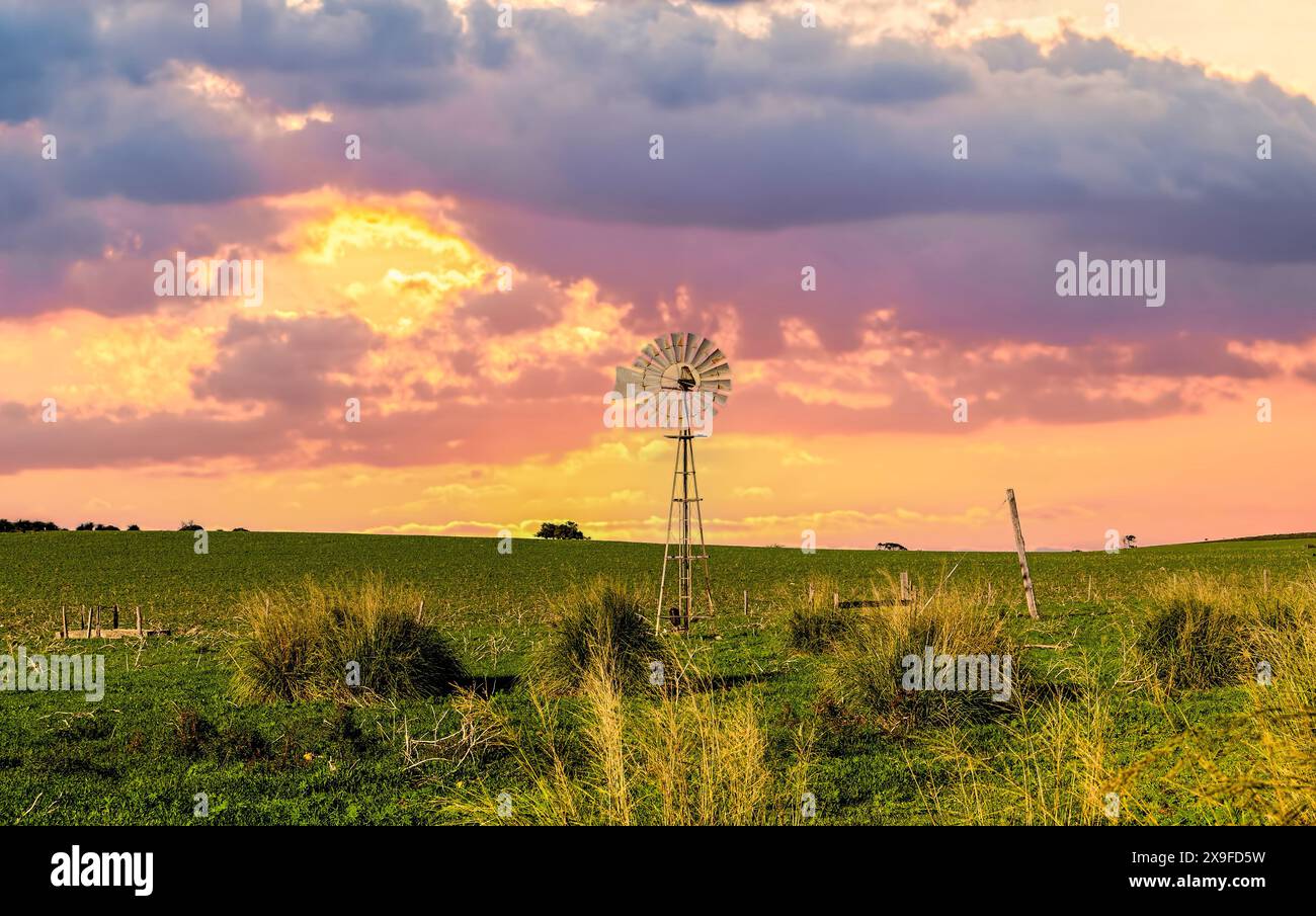 Sunset over a traditional metal windmill in rural outback landscape ...