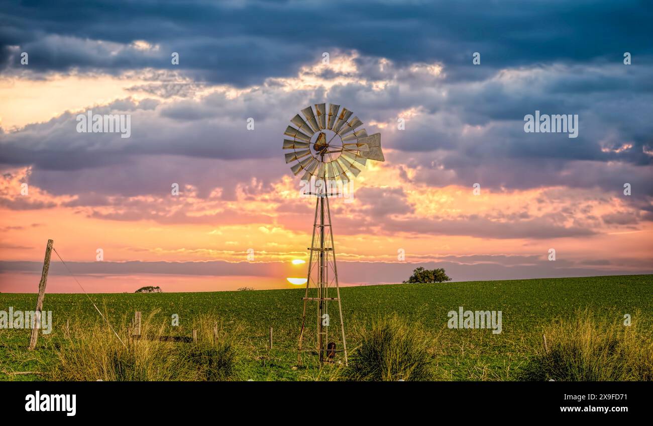 Sunset over a traditional metal windmill in rural outback landscape ...