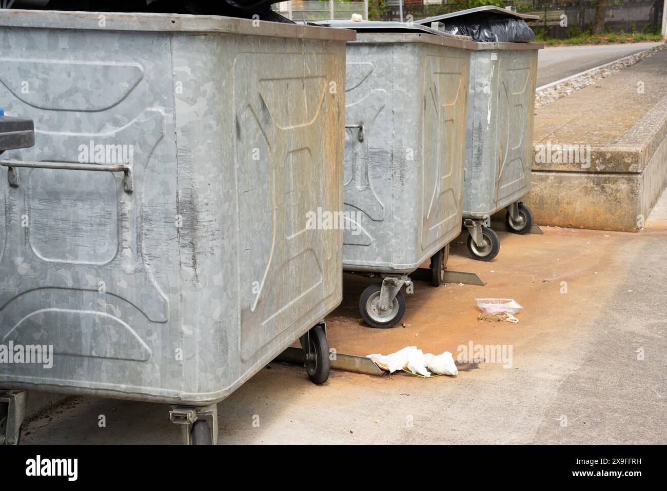 Three trash containers on wheels with trash left carelessly in front of ...