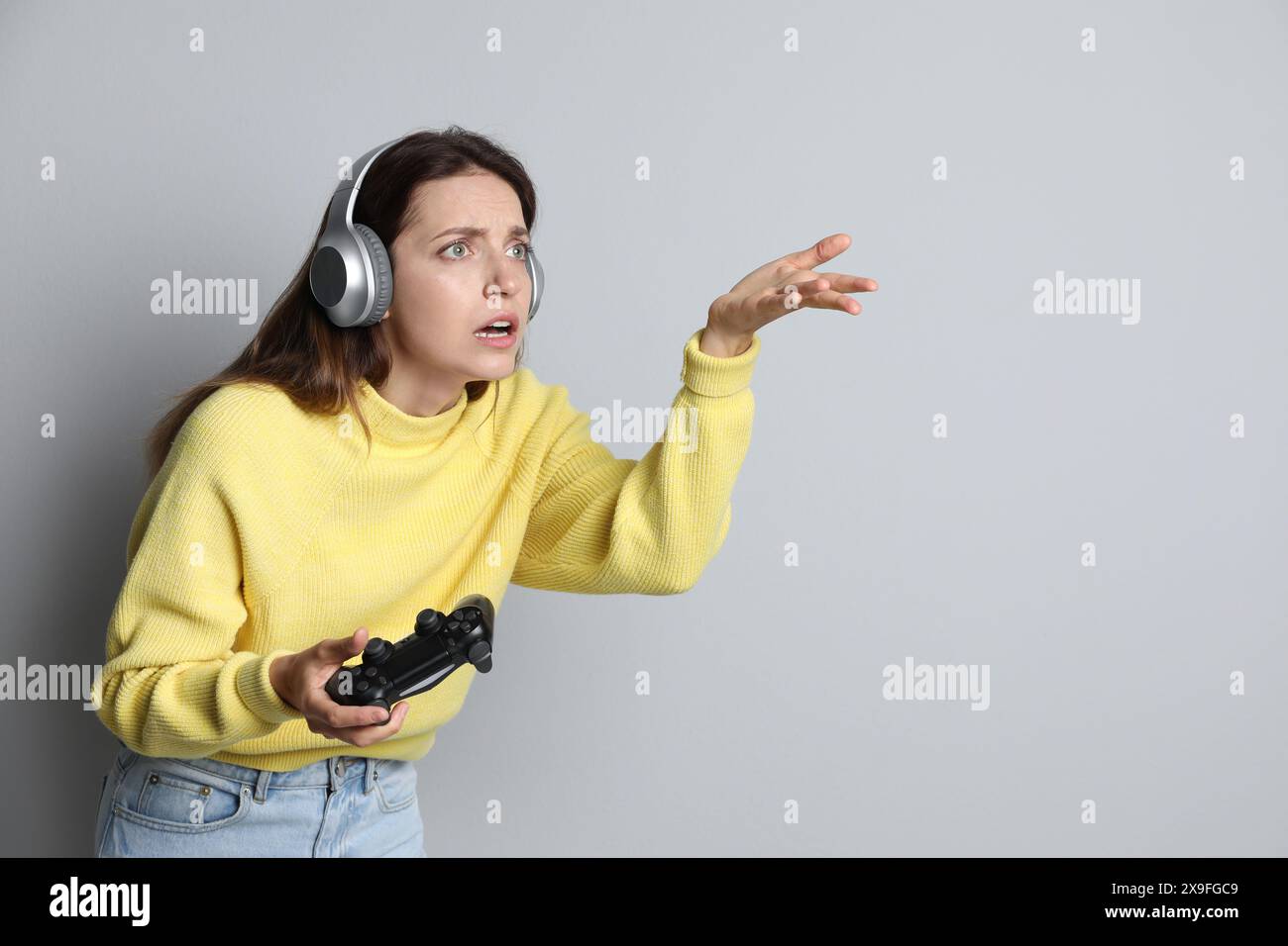 Confused woman in headphones with game controller on light grey ...