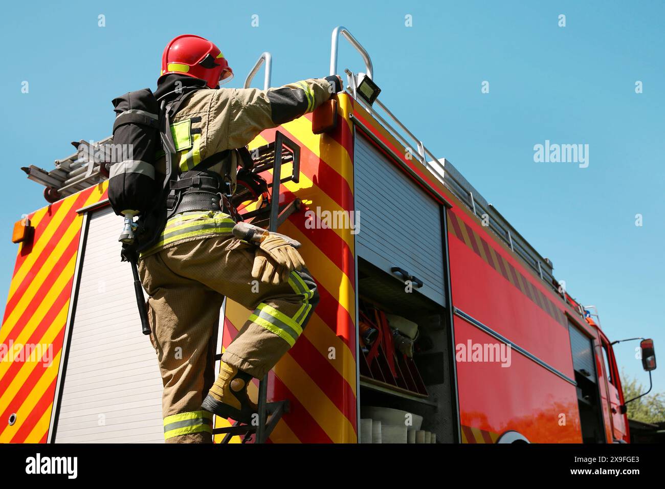Firefighter in uniform on fire truck outdoors, back view Stock Photo ...