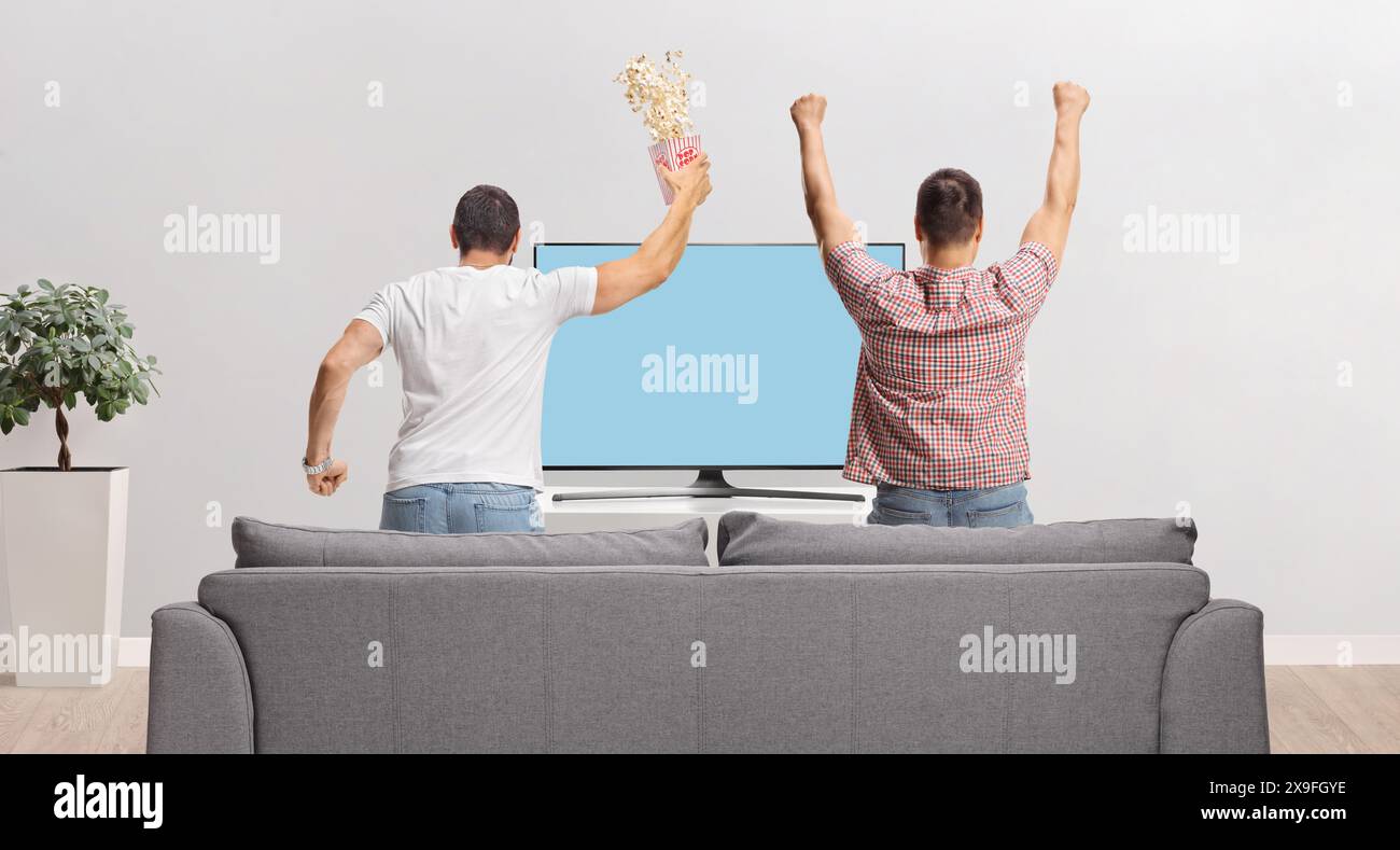 Rear view shot of young men watching football match on tv and jumping ...